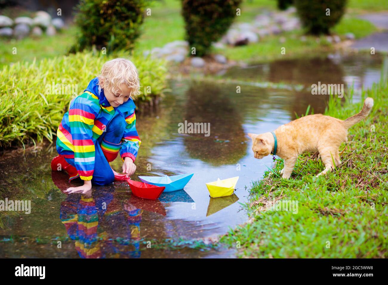 Child and cat playing with paper boat in puddle. Kids play outdoor by ...