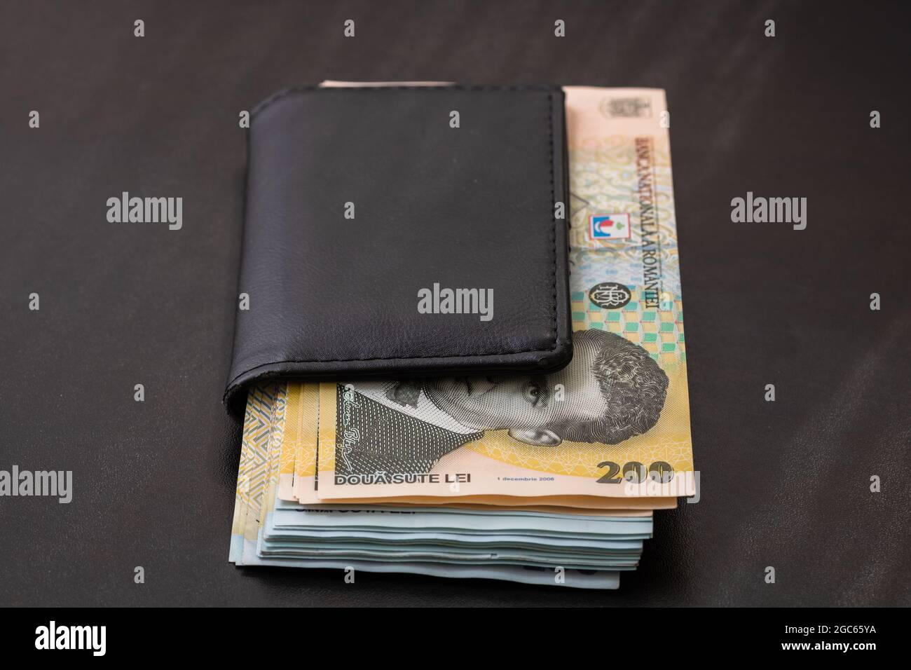 Small black wallet with a bigger bundle of Romanian Leu on the table ...
