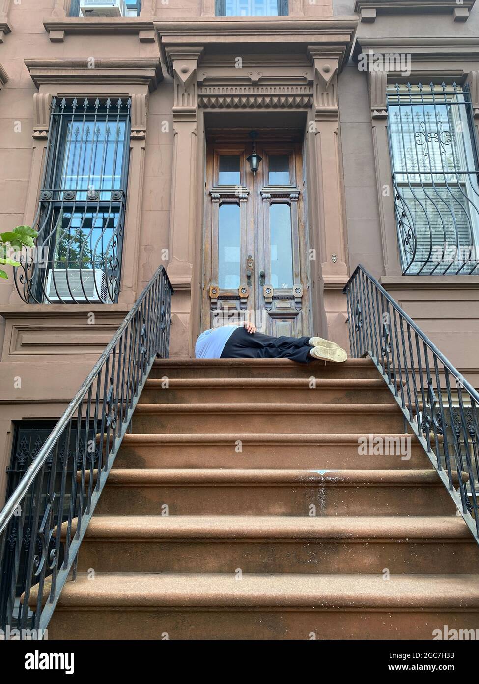 Homeless man sleeps just outside the door of a high stoop brownstone ...