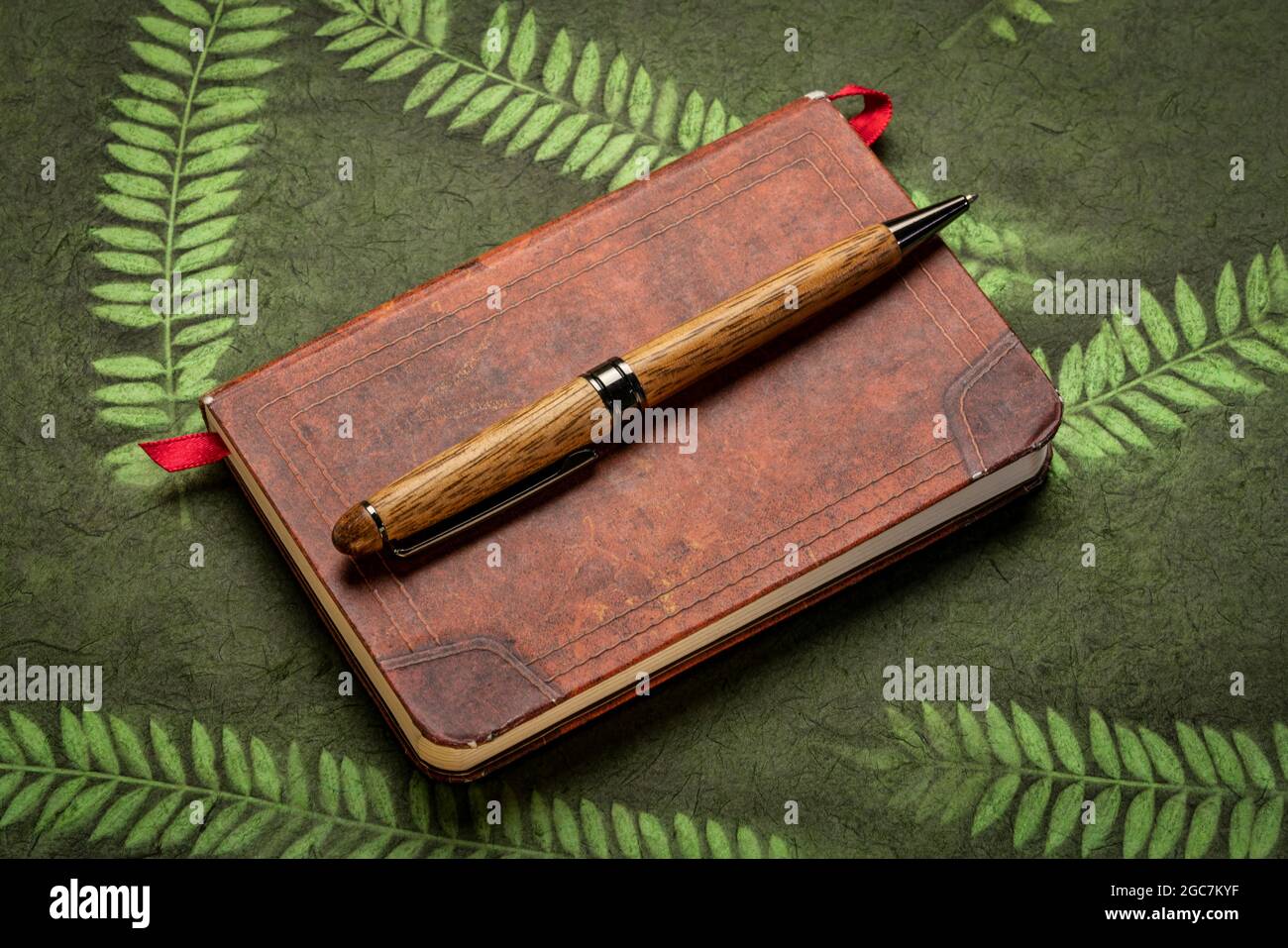 small leather-bound journal with a stylish pen against green paper with ...