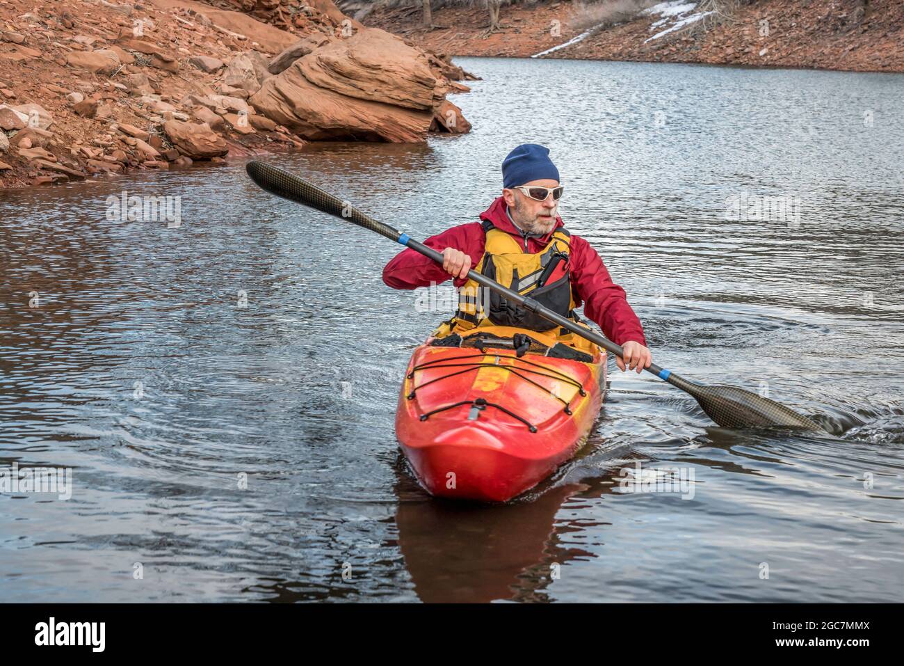 senior male paddler is paddling colorful river kayak on a calm lake ...