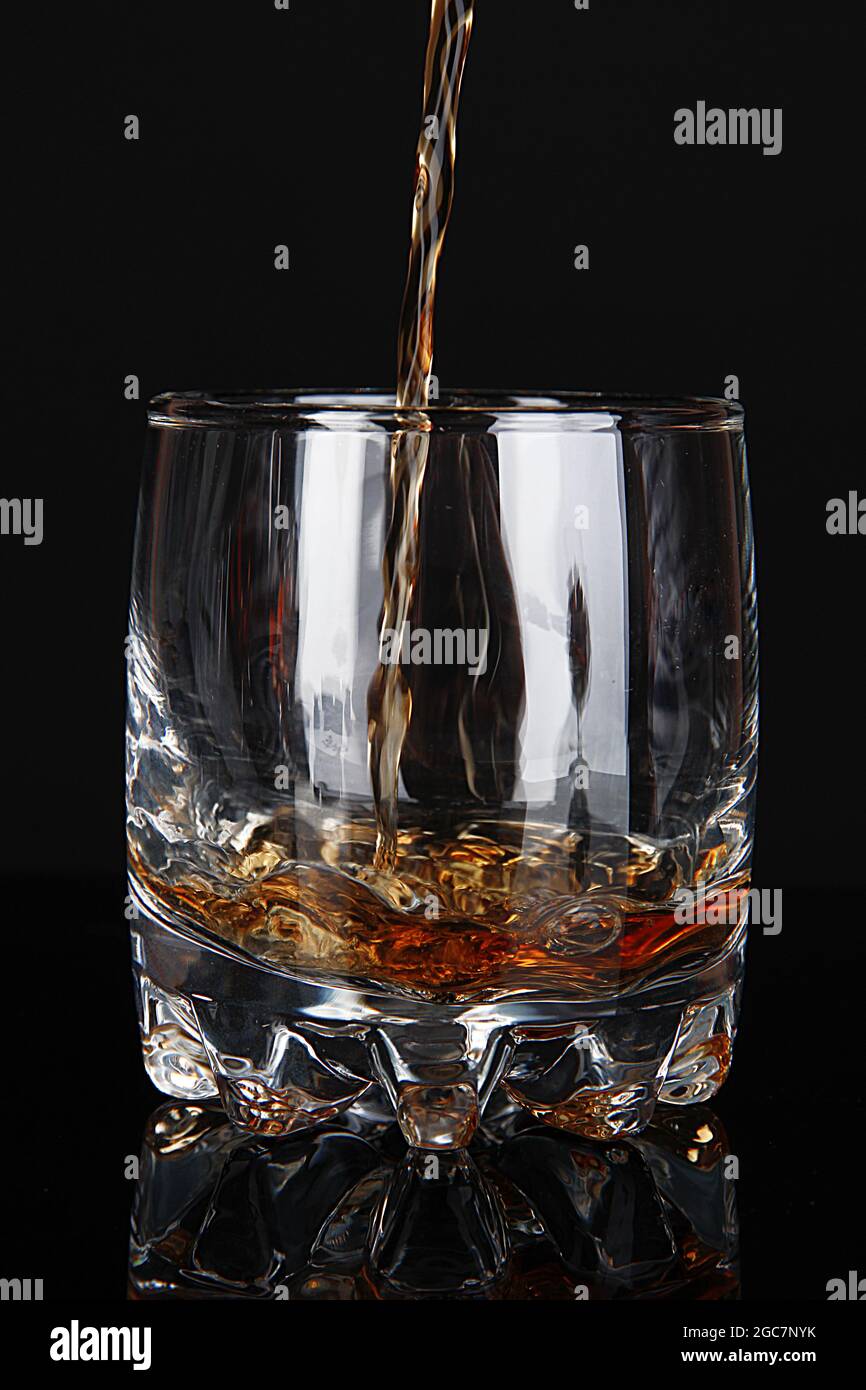 Brandy pouring into glass on black background Stock Photo - Alamy