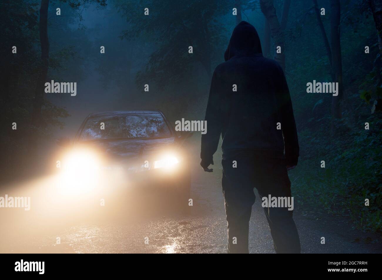 A spooky hooded figure silhouetted against a cars headlights. On a ...