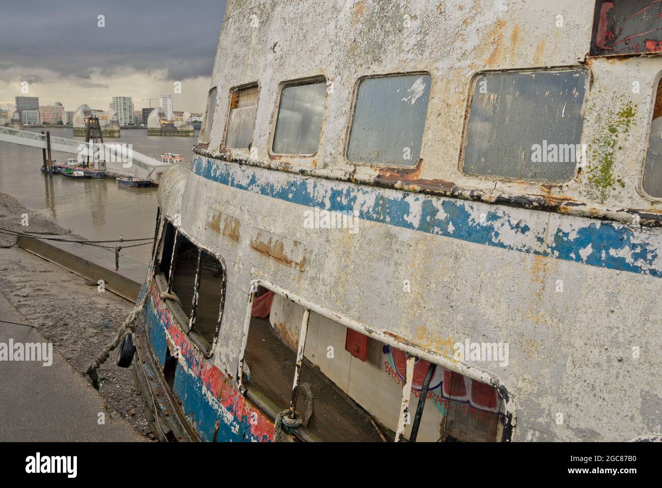 Rusty ship hull of old Mersey ferry by river Thames barrier opposite ...