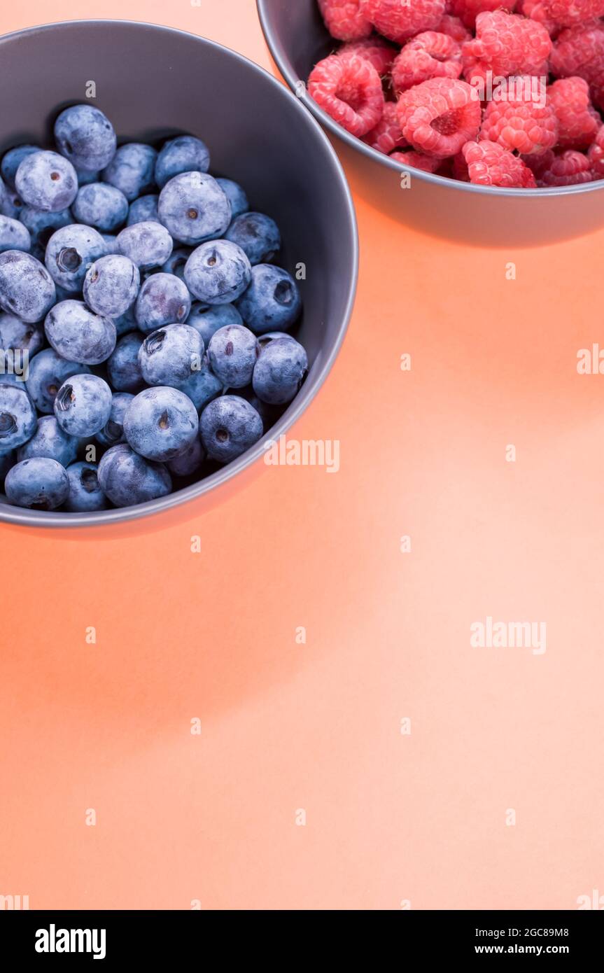 Bowls of raspberries and blueberries isolated on a peach background ...