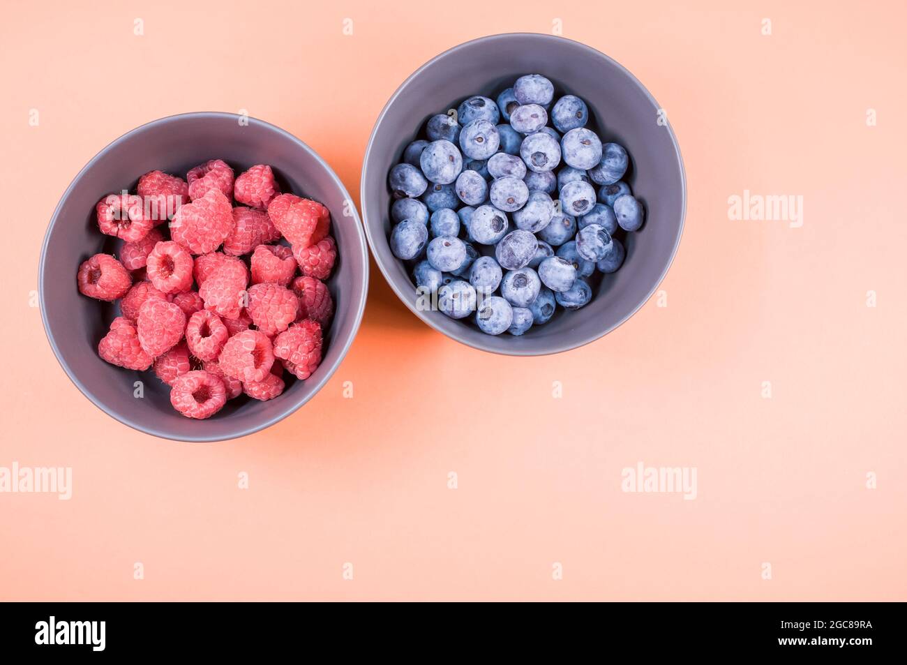 Bowls of raspberries and blueberries isolated on a peach background ...