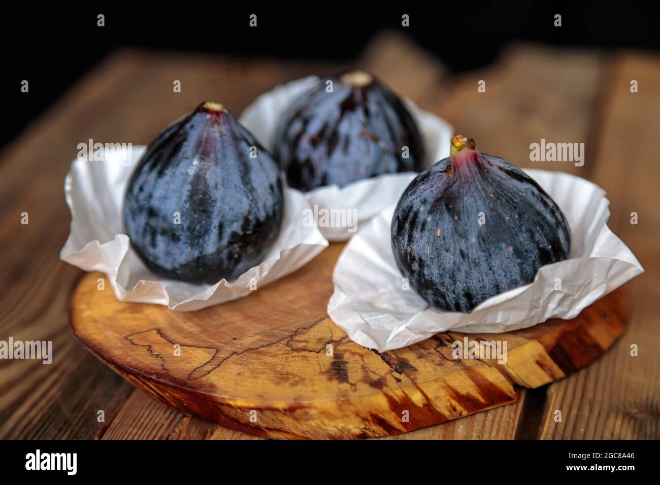 Fresh purple figs are wrapped in paper, on a wooden background from old ...