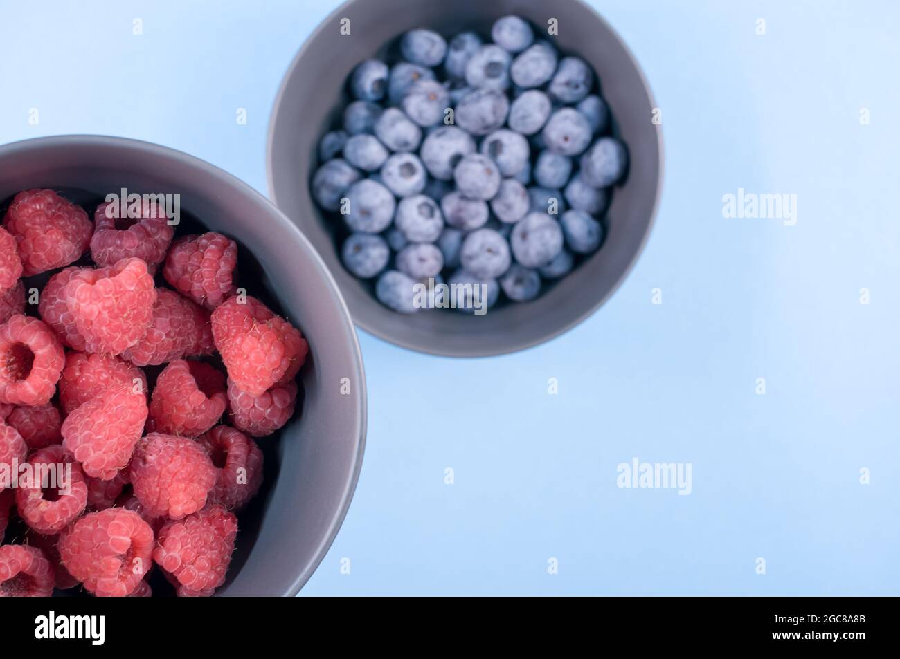 Bowls of raspberries and blueberries isolated on a blue background with ...