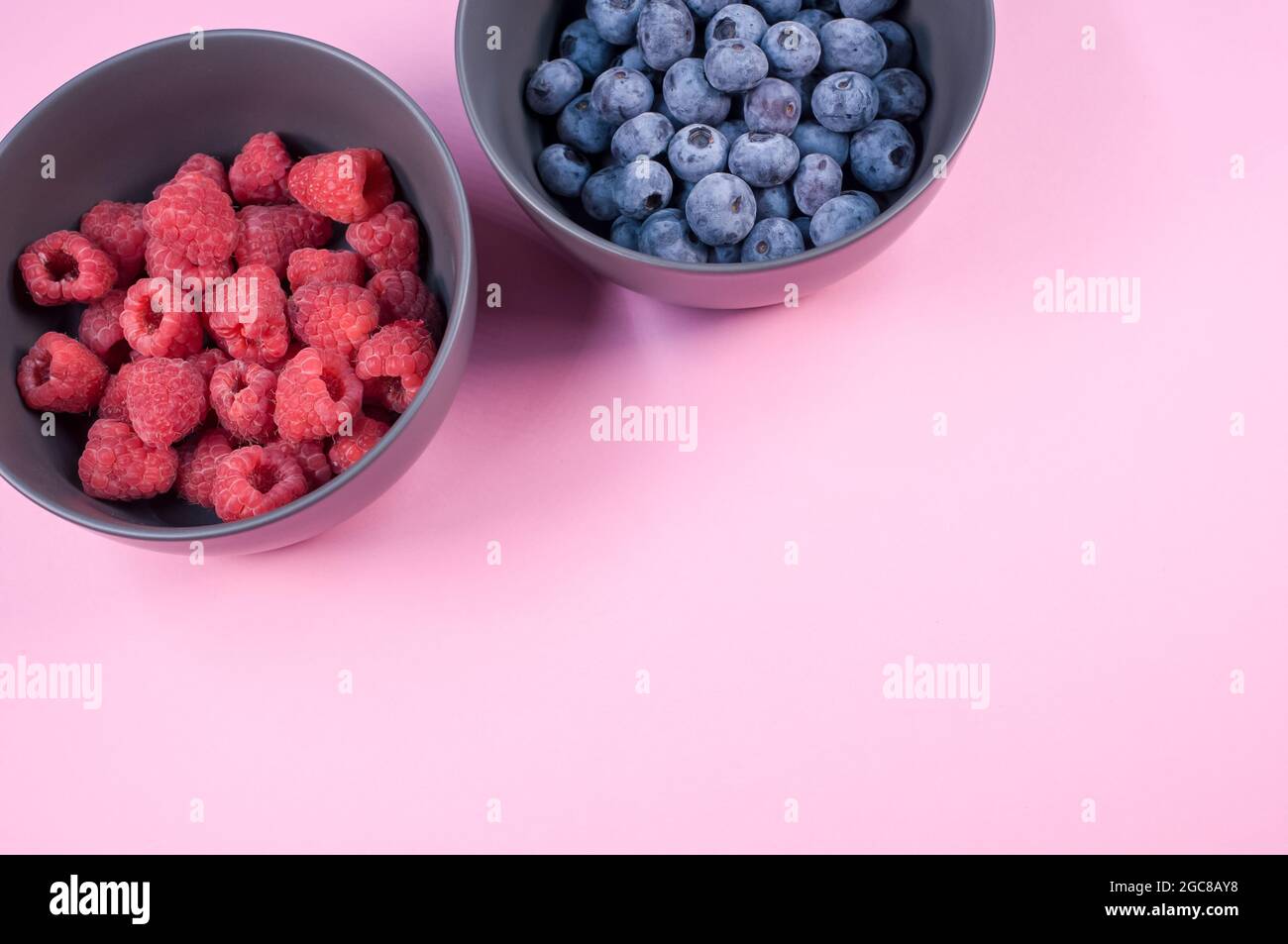 Bowls of raspberries and blueberries isolated on a pink background with ...