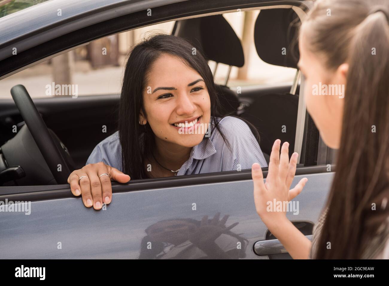 Young mother smiling out of the car to her daughter who waves goodbye ...