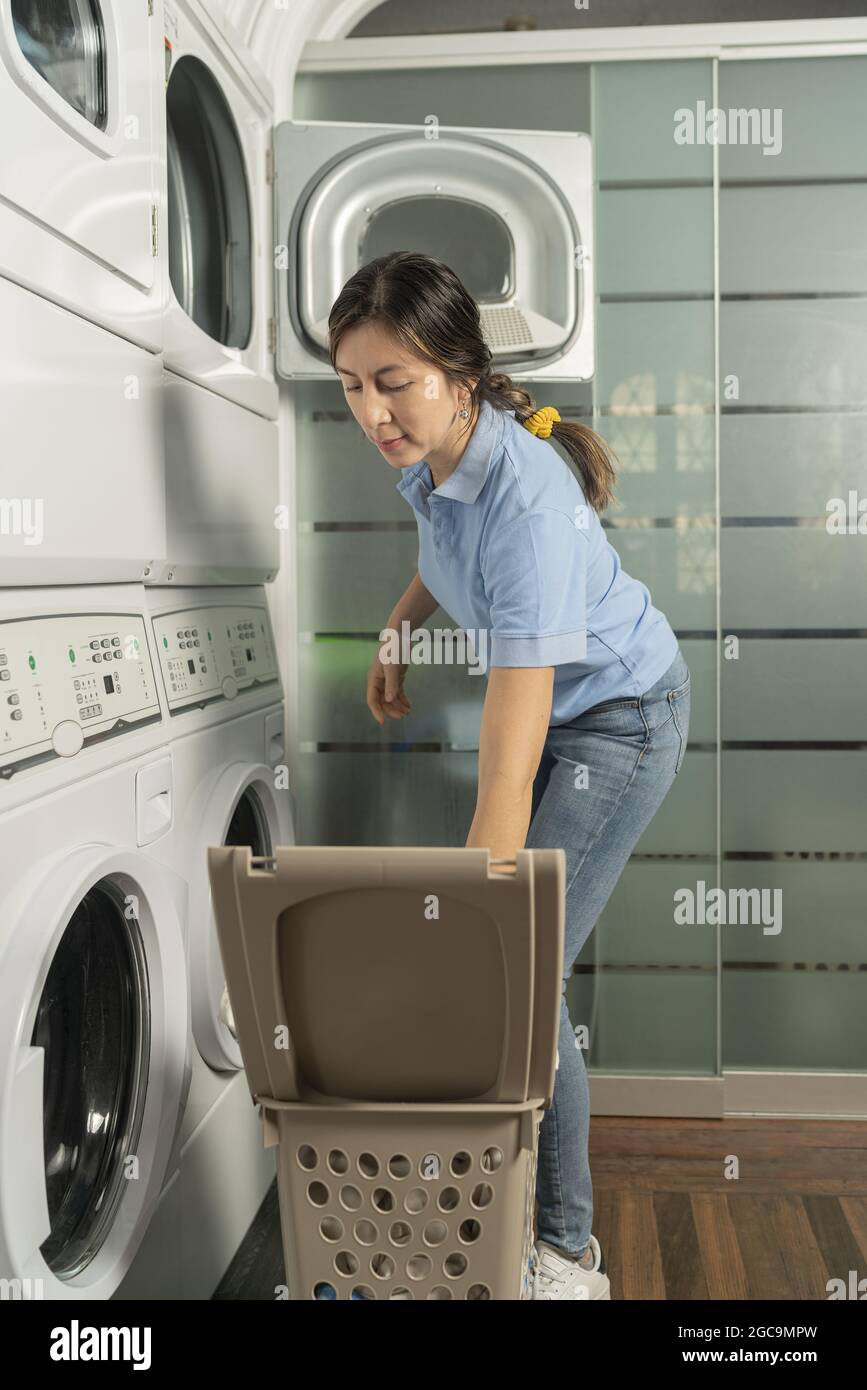 Vertical shot of a laundry worker taking clothes out of a basket to be washed in washing machine ...