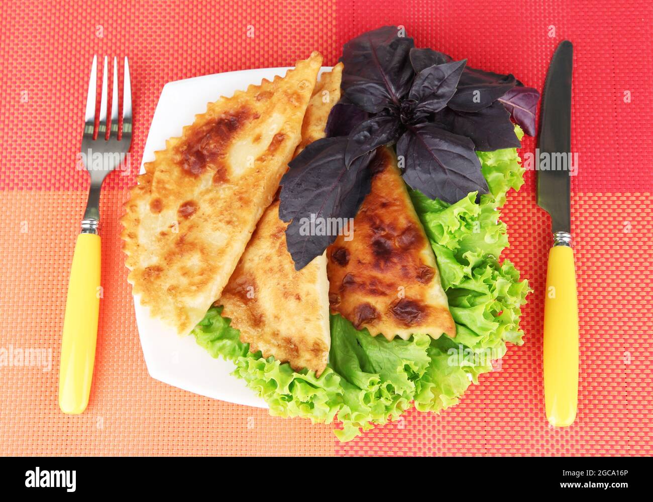 Tasty chebureks with fresh herbs on plate,on color napkin background ...