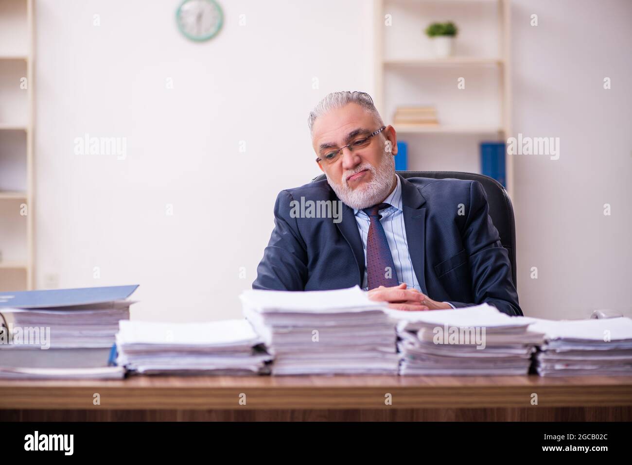Old male employee unhappy with excessive work at workplace Stock Photo ...
