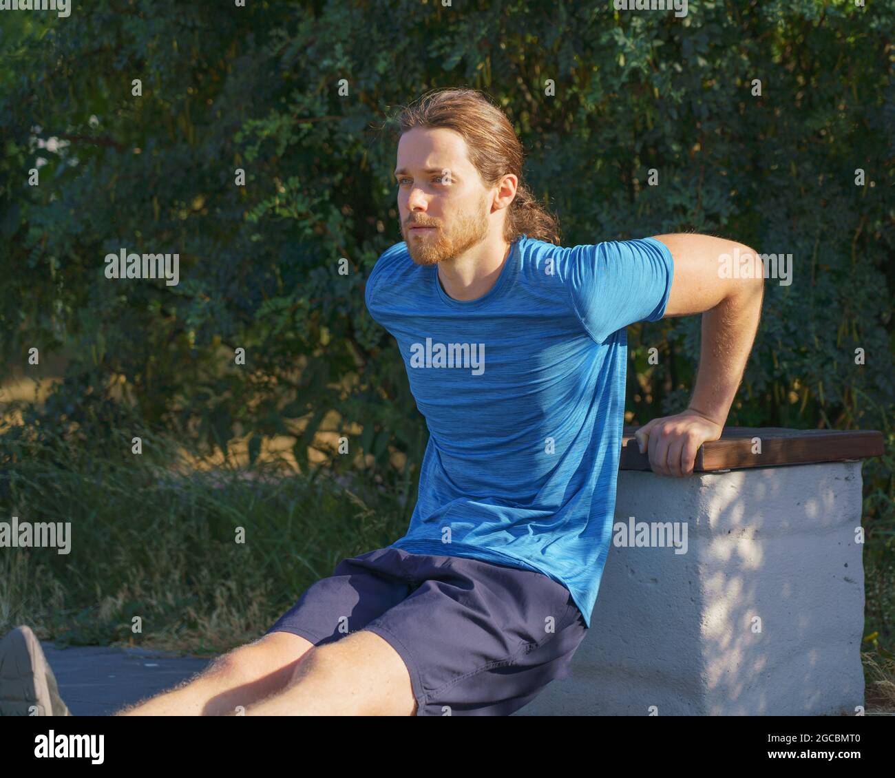 Sportive guy training triceps while doing push ups on bench in park on ...