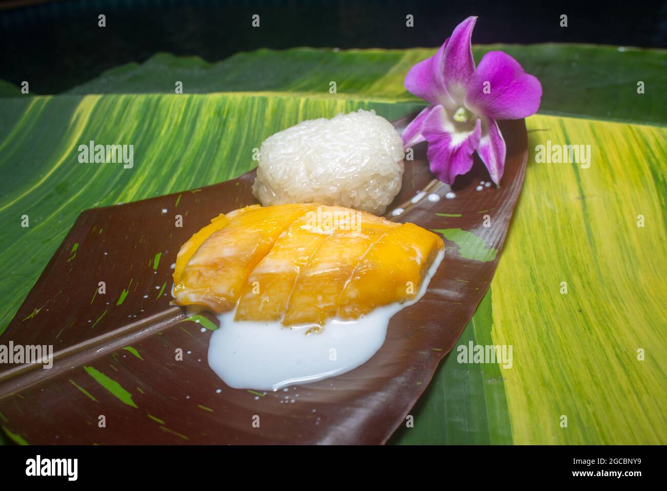Mango sticky rice served on a spotted banana leaf by the pool. speckled ...
