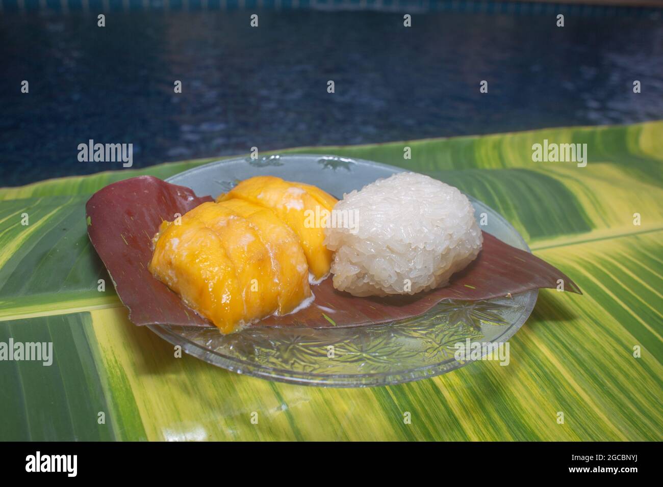 Mango sticky rice served on a spotted banana leaf by the pool. speckled ...