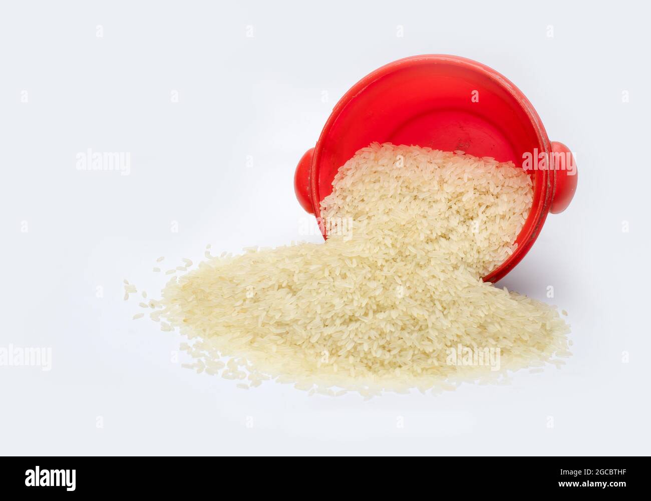 Uncooked dry rice fell from a small red bowl on an isolated white ...
