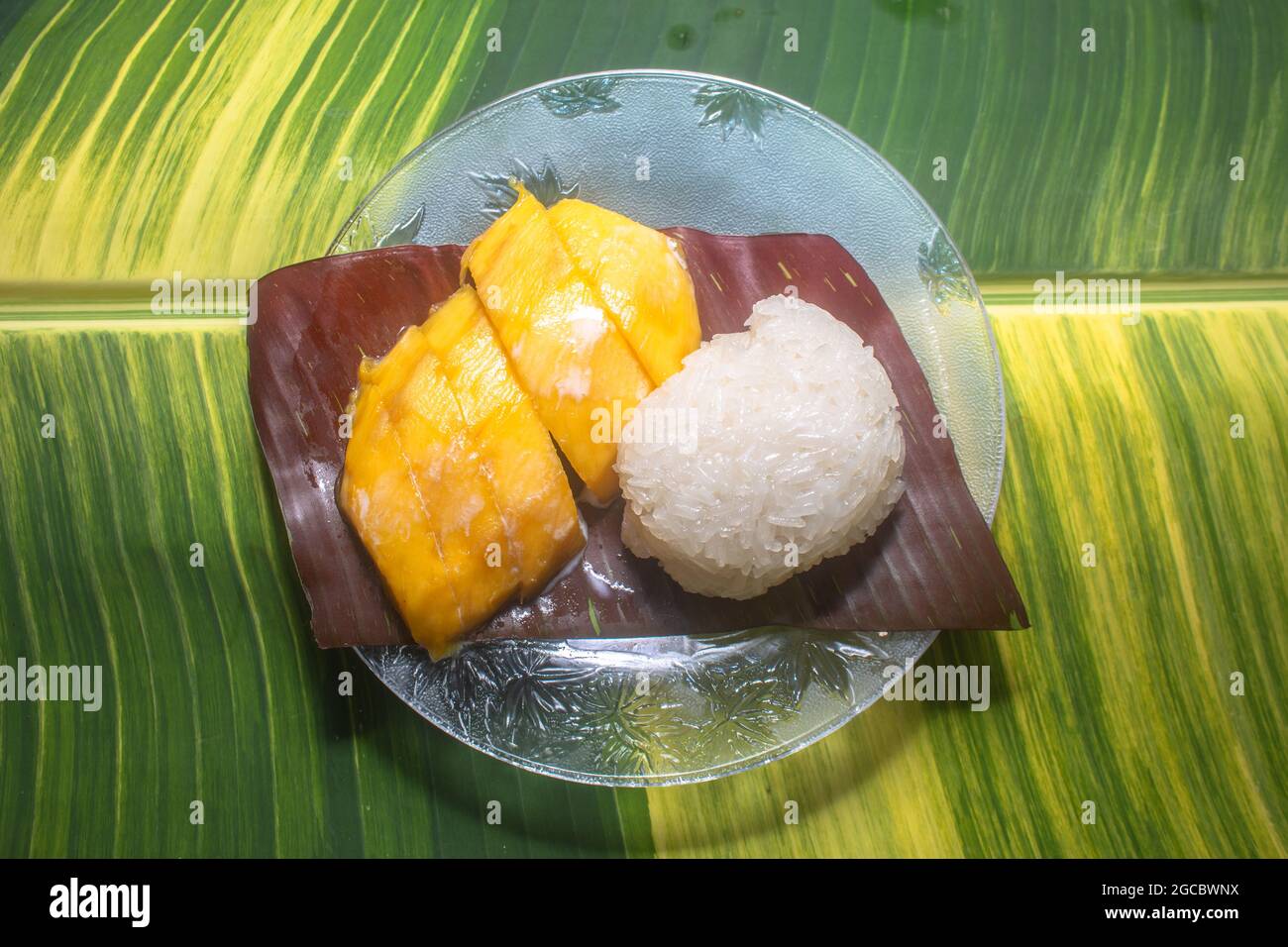 Mango sticky rice served on a spotted banana leaf by the pool. speckled ...