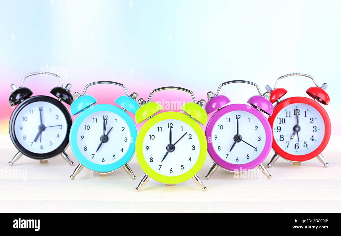 Colorful alarm clocks on table on light background Stock Photo - Alamy