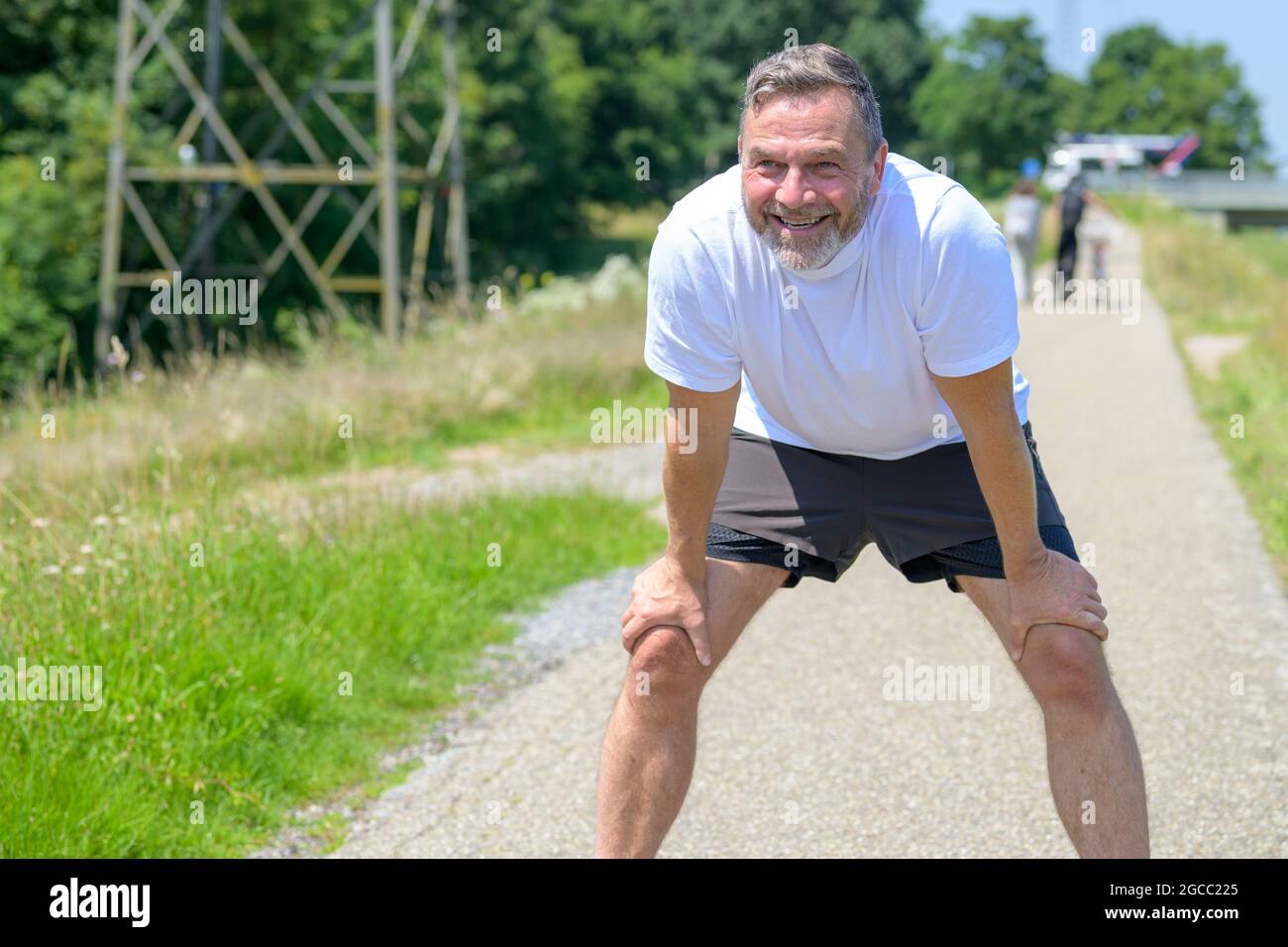 Happy healthy man taking a rest while out jogging leaning forwards on ...