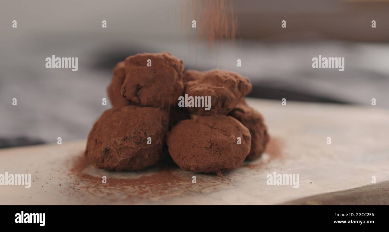 sprinkle cocoa powder over handmade chocolate truffles on a wood board ...