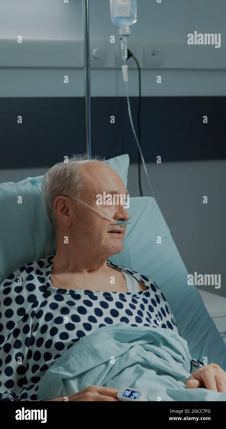 Nurse checking file of sick patient laying in hospital ward bed at ...