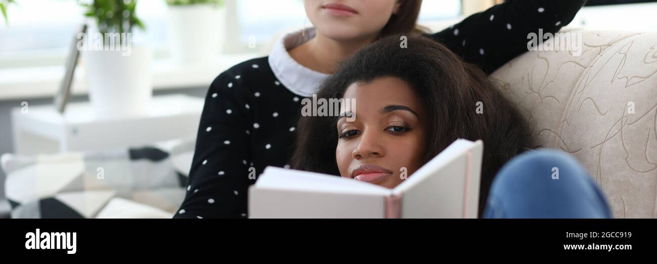 Two women on couch are reading book Stock Photo - Alamy
