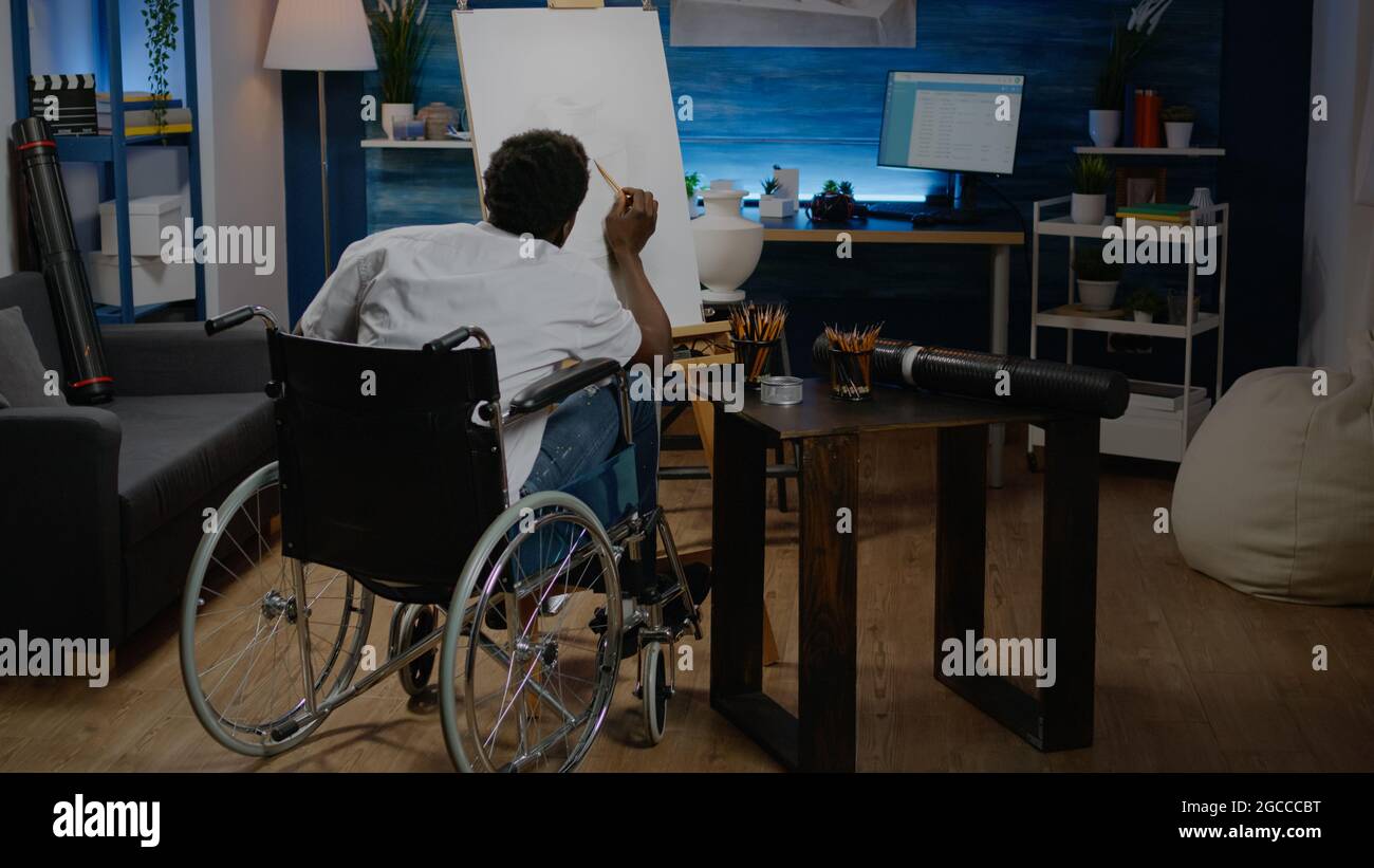 Black young artist with handicap drawing vase on canvas and easel at ...