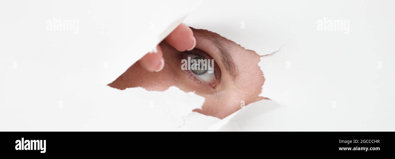 Female eye looks through hole in white paper Stock Photo - Alamy