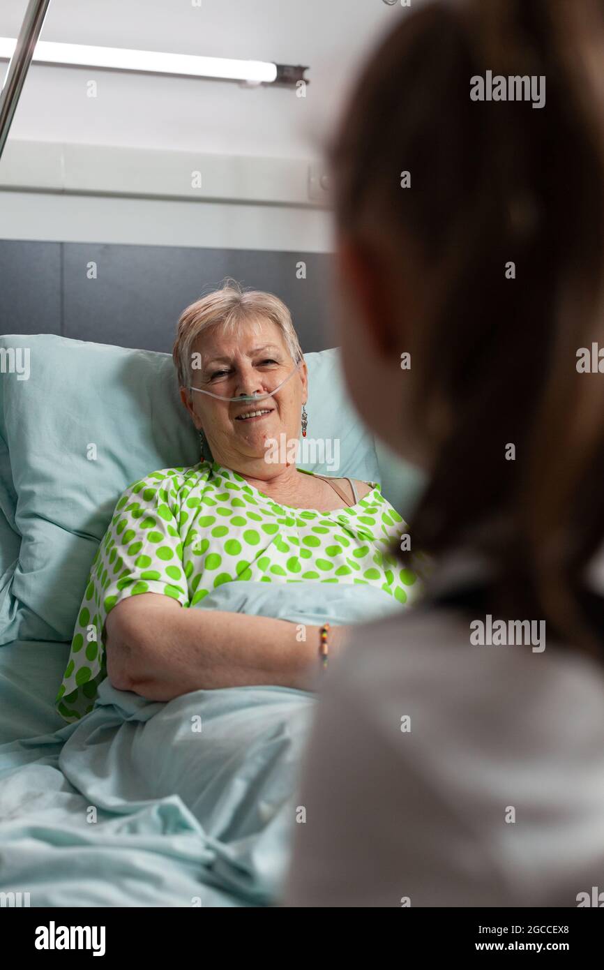 Sick retired grandmother talking with grandchild while resting in bed ...