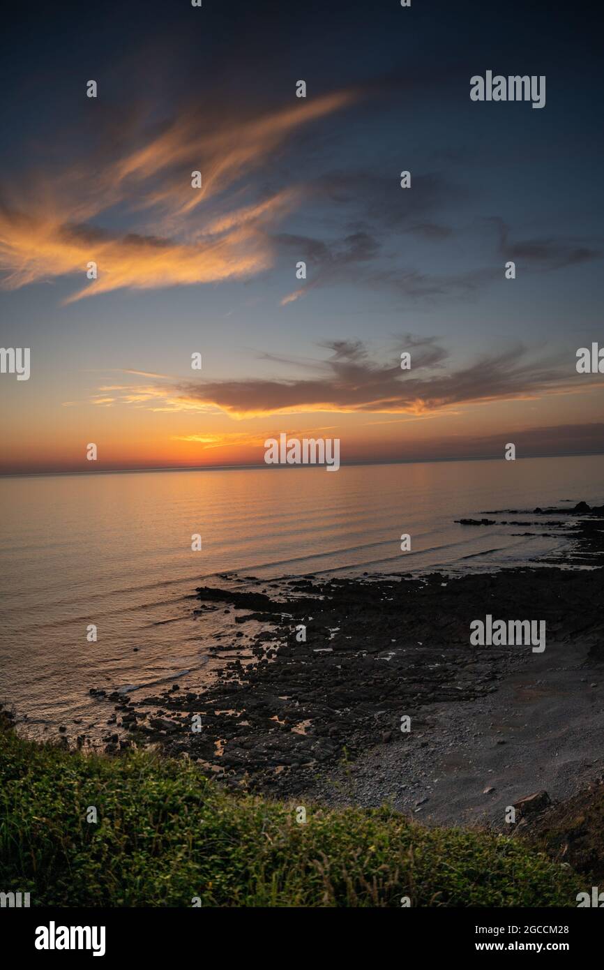 Dramatic sunset over calm sea with golden clouds and rocky coastline ...