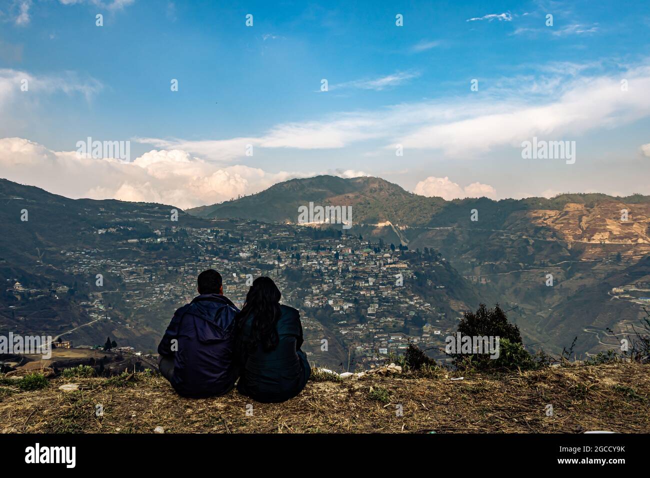 couple sitting at mountain top edge with crowded city structure and ...