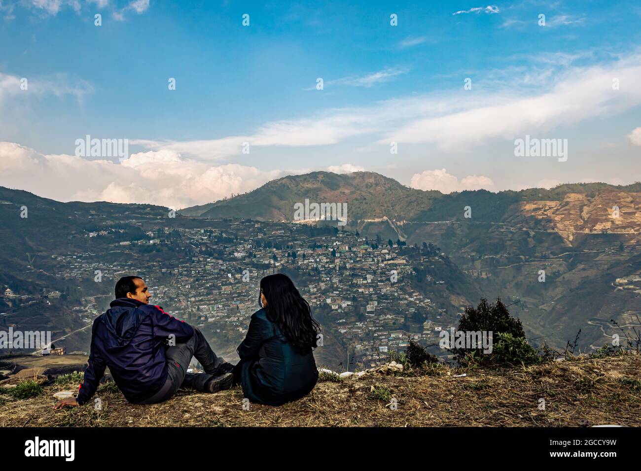 couple sitting at mountain top edge with crowded city structure and ...