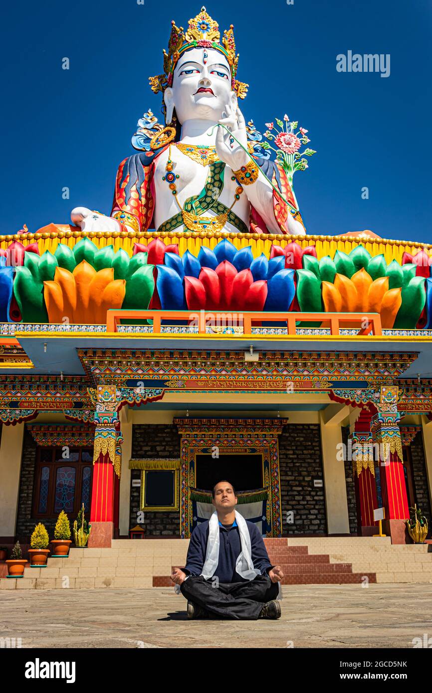 young man meditating in front of buddhist colorful goddess statue with ...