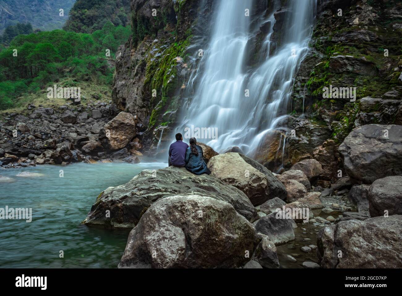 couple sitting at rock in front of waterfall white water stream falling ...