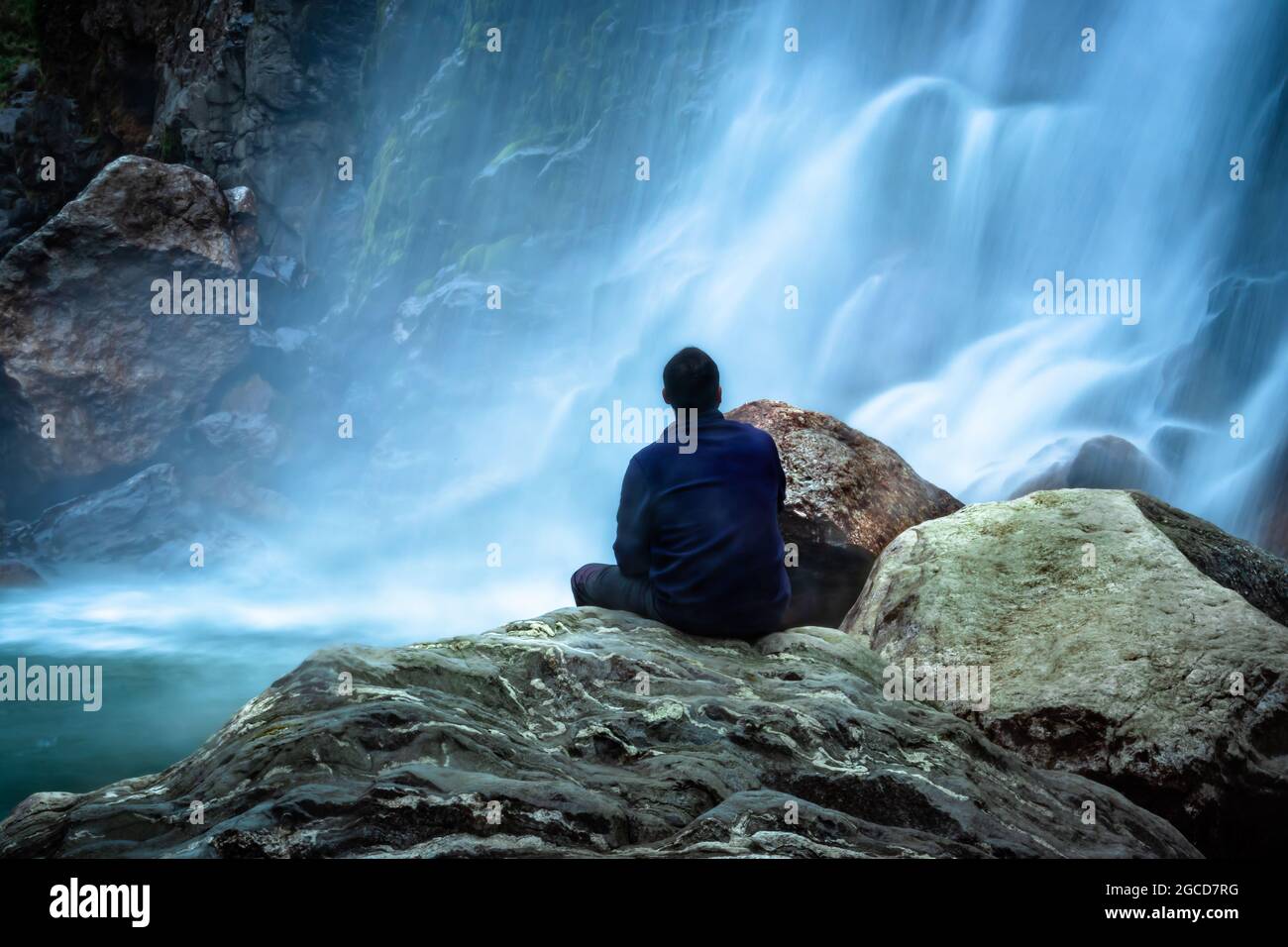man sitting at rock in front of waterfall white water stream falling ...