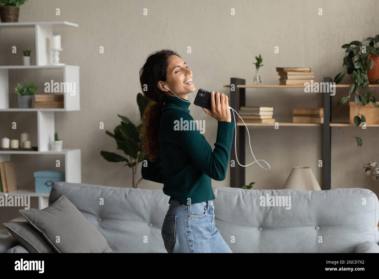Happy attractive woman in earphones holding smartphone, dancing alone ...