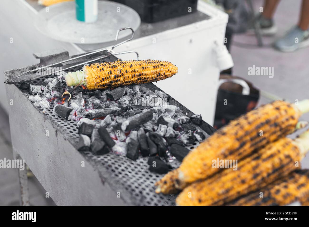 Several ears of corn roasting over charcoal at a street food stall ...
