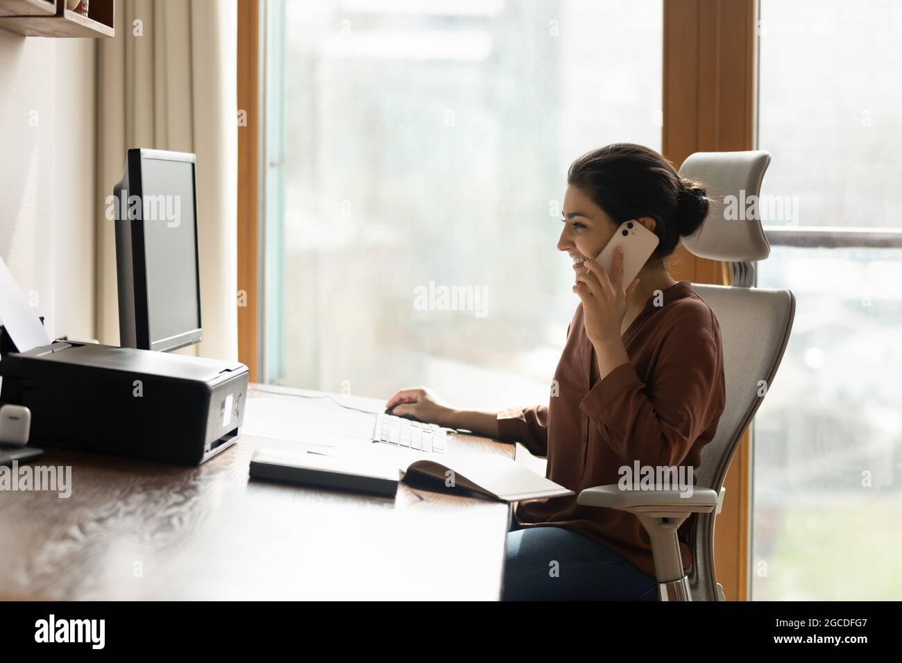 Smiling Indian woman work on computer talk on cell Stock Photo - Alamy