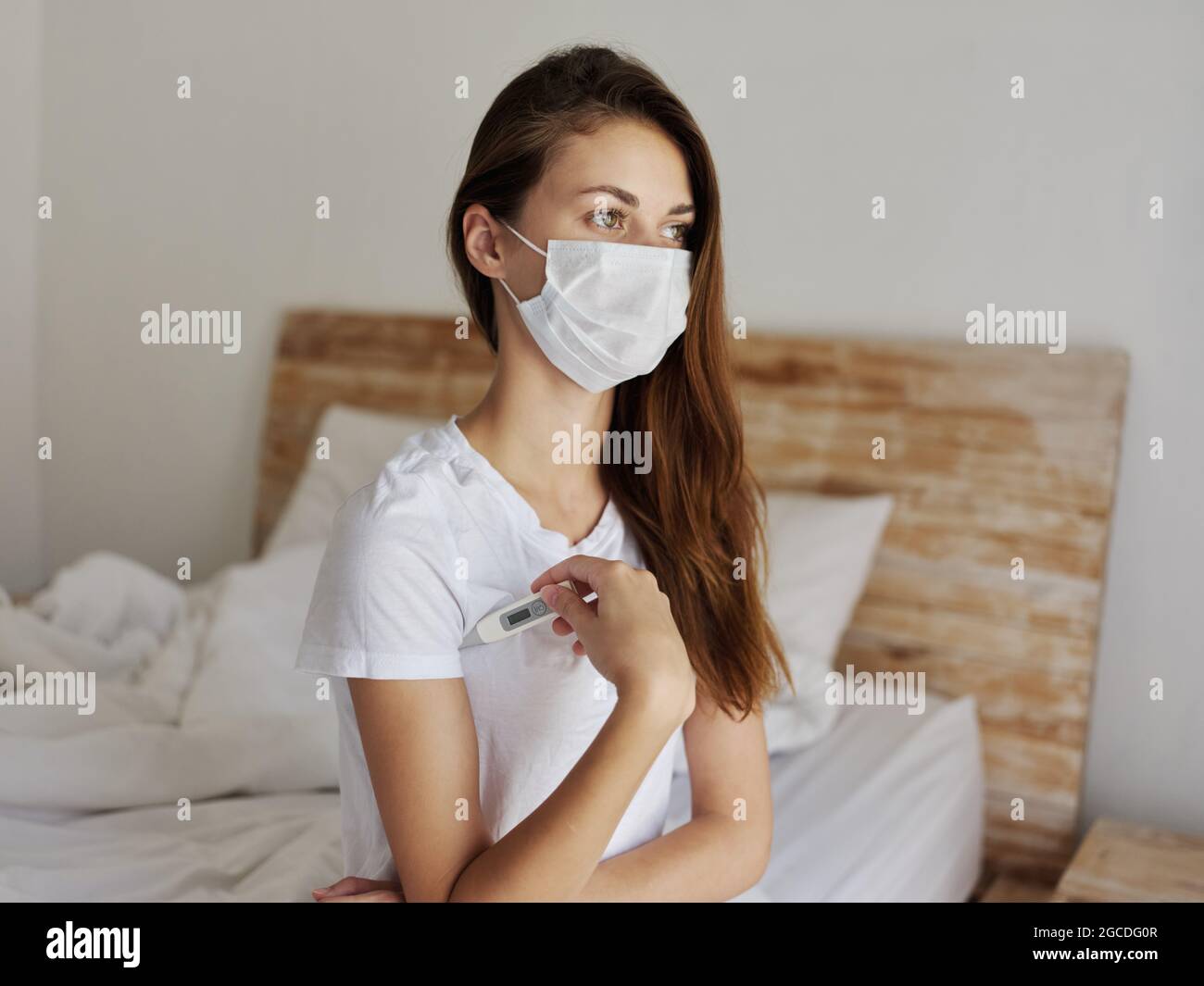 woman with thermometer under her arm wearing medical mask checking ...