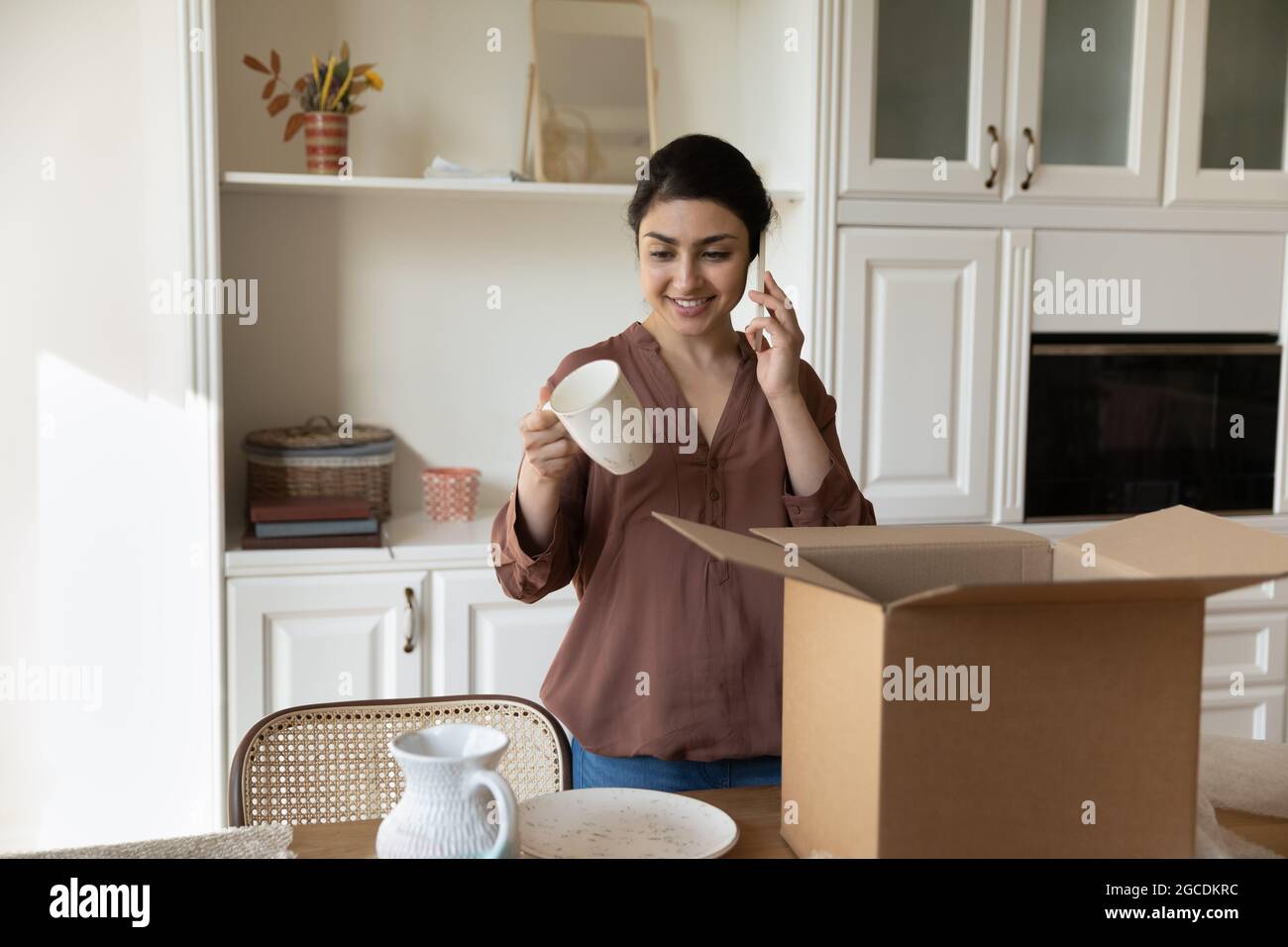 Smiling ethnic female renter unpack parcel with kitchenware Stock Photo ...