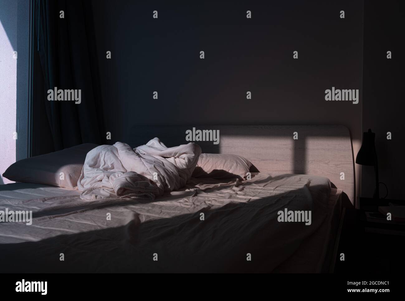 An unmade empty bed in the dramatic dim light coming from a window ...