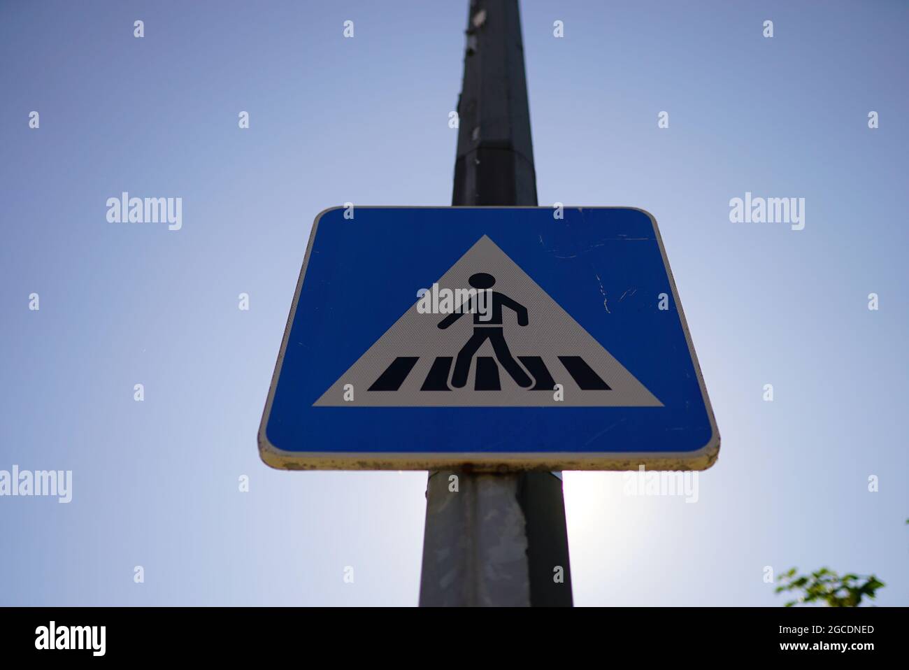 A pedestrian crossing road sign on the metal post in the blue sky ...