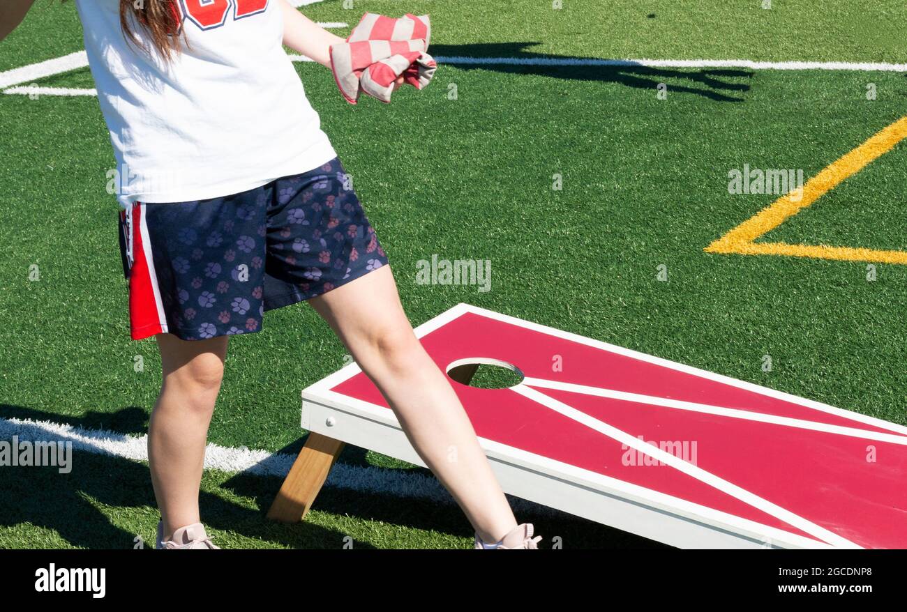 Side view of a girl throwing a bean bag playing cornhole standing on ...