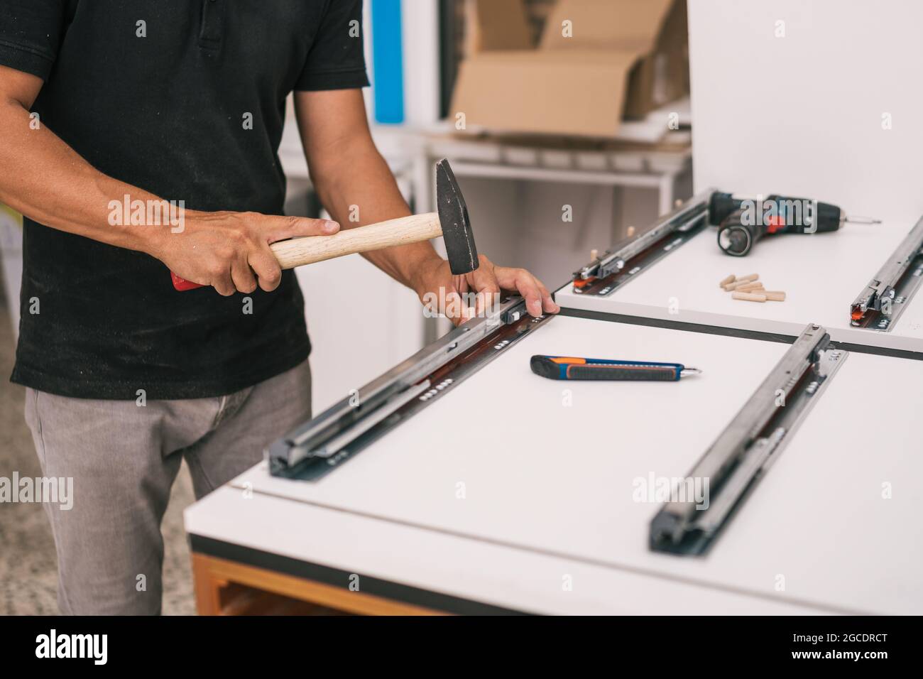 Man fixing a rail on a piece of furniture with a hammer in a workshop ...