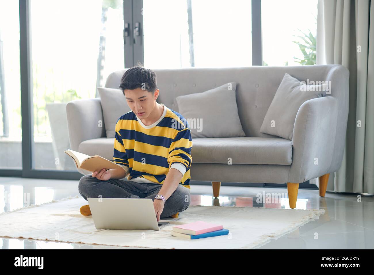 Attractive happy smart young man sitting on a floor in the living room ...