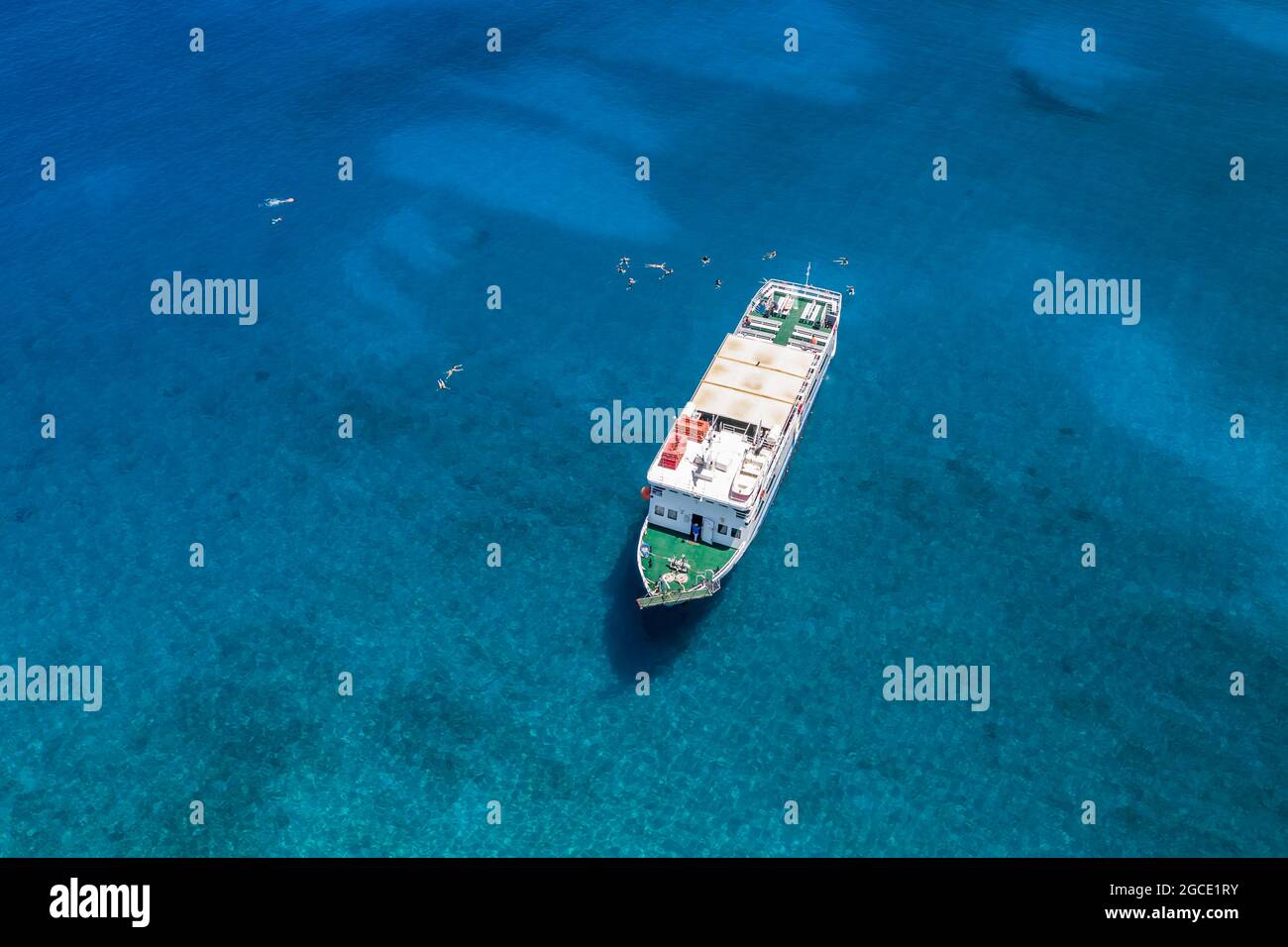 Aerial view of swimmers and snorkelers around a boat in a crystal clear ...