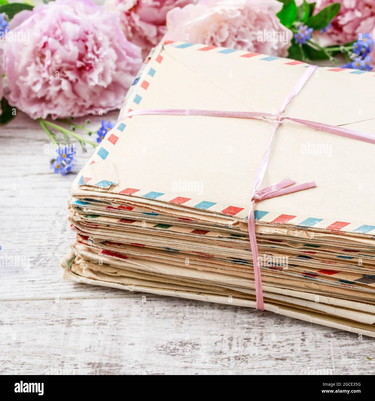 Stack of vintage love letters and pink peonies in the background. Retro ...