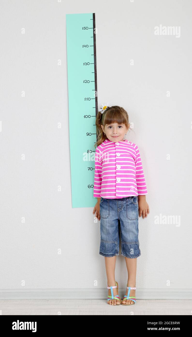 Little girl measuring height against wall in room Stock Photo - Alamy