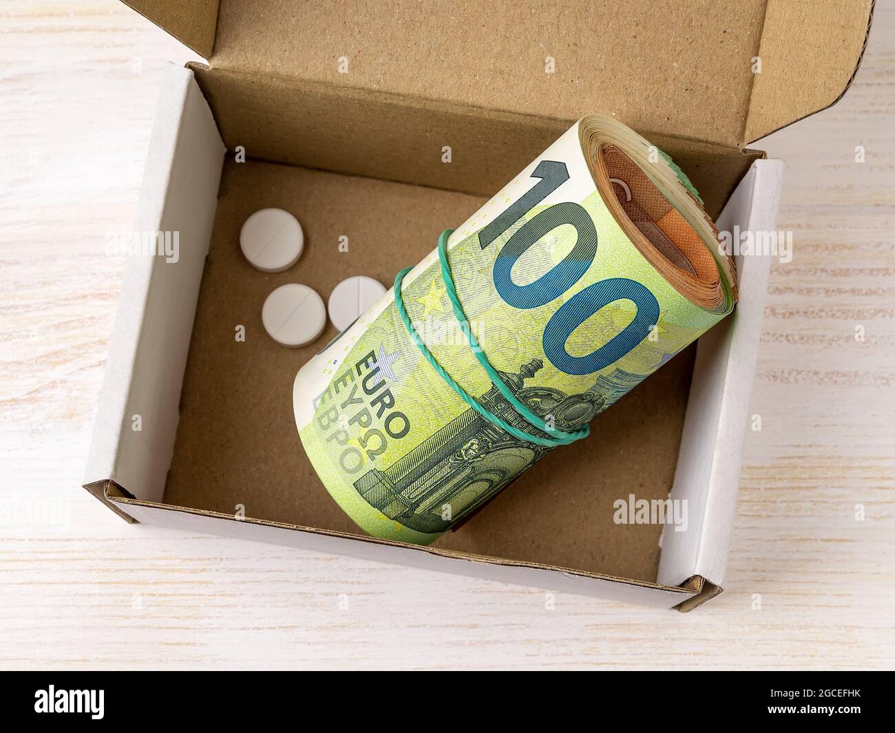 Roll of 100 euro banknotes and few pills in an open small cardboard box ...